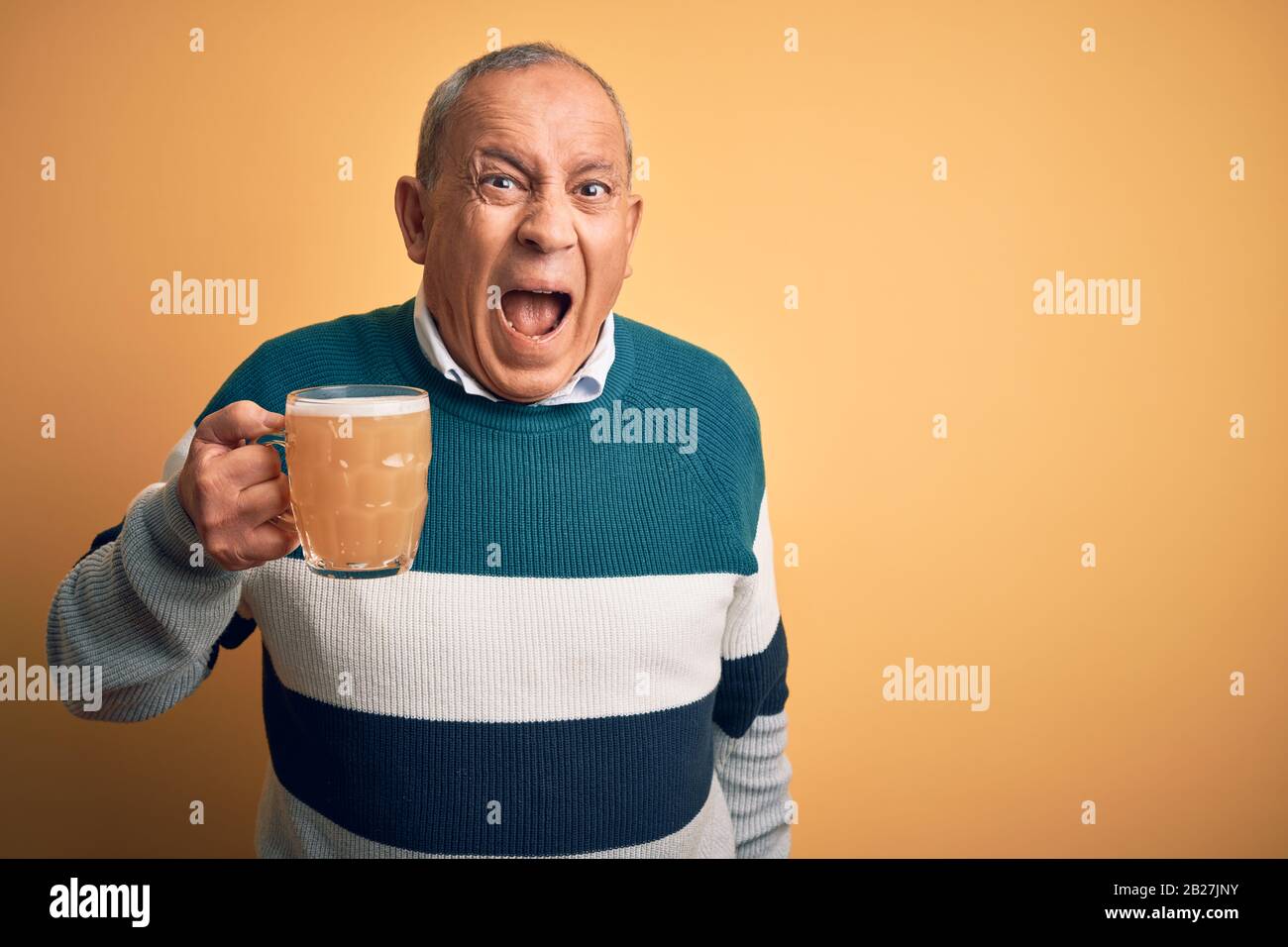 Senior handsome man drinking jar of beer standing over isolated yellow ...