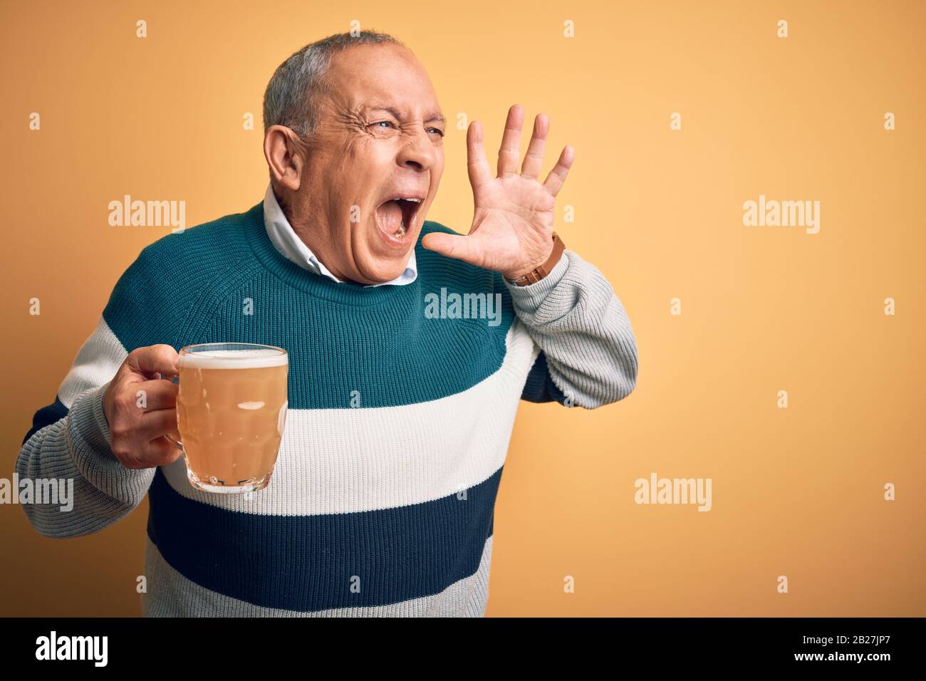 Senior handsome man drinking jar of beer standing over isolated yellow ...