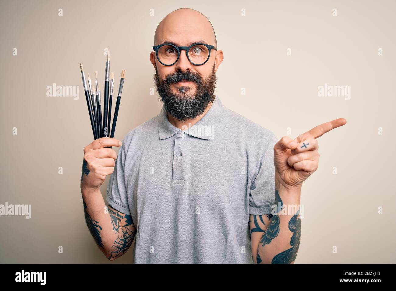 Handsome bald artist man with beard and tattoo painting using painter ...