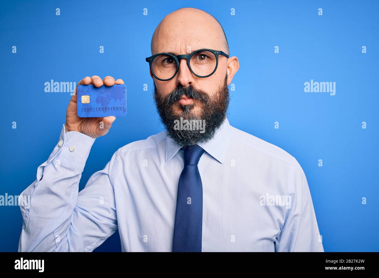 Handsome bald business man with beard holding credit card over isolated ...