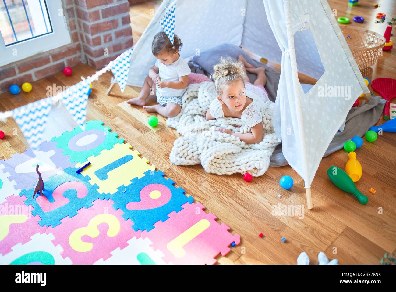 Beautiful toddlers playing inside tipi over blanket around lots of toys ...