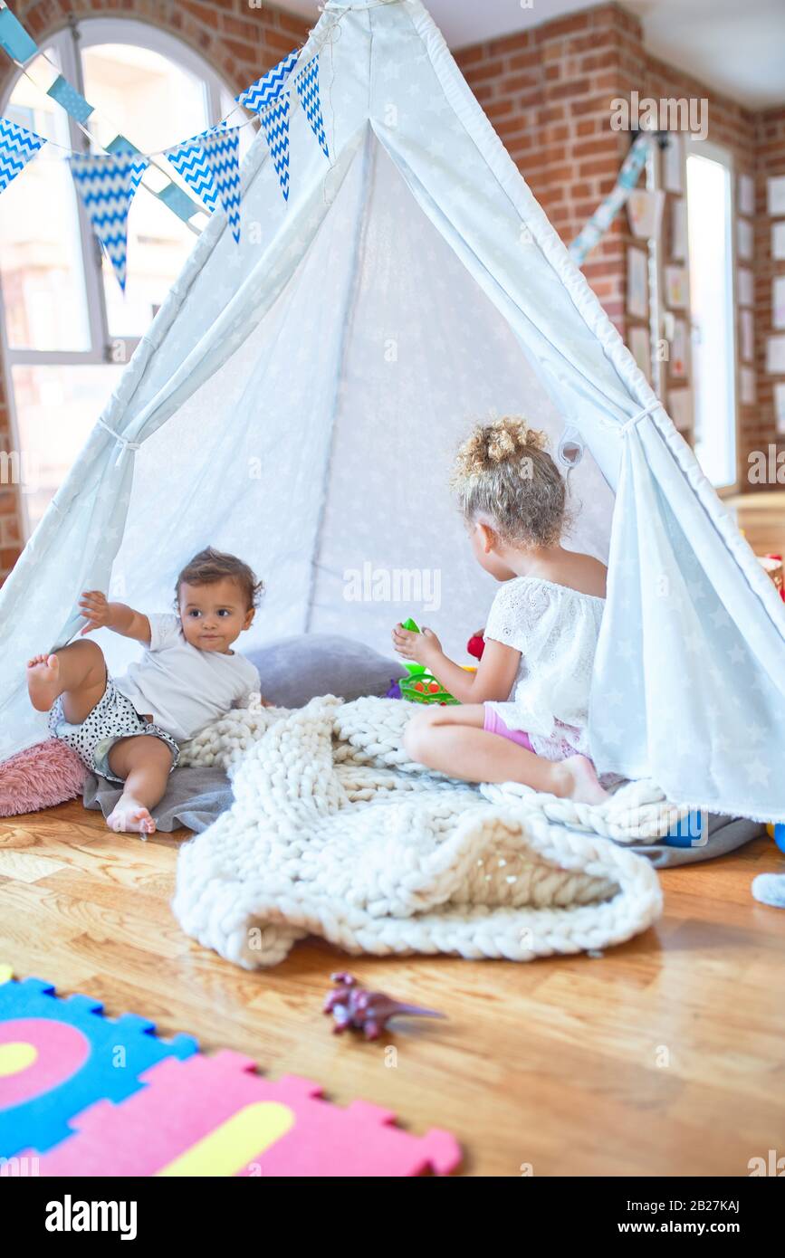 Beautiful toddlers playing inside tipi over blanket around lots of toys ...