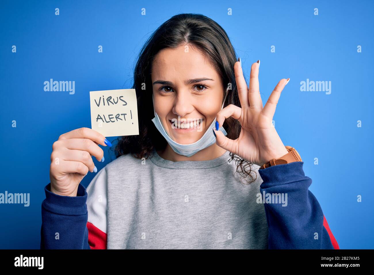 Young beautiful woman with curly hair wearing mask holding reminder ...