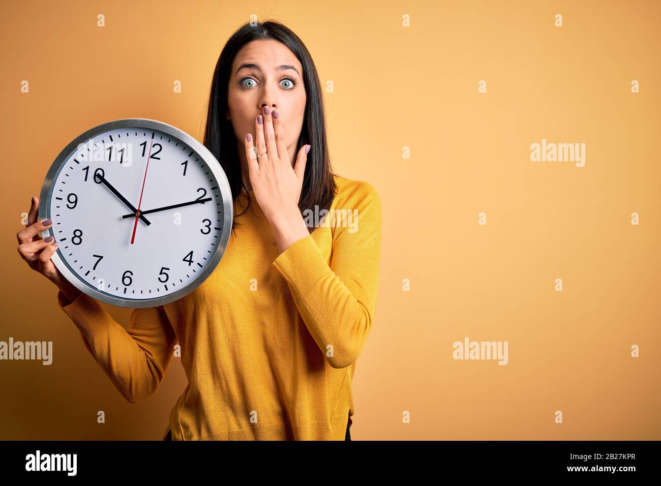 Young woman with blue eyes doing countdown holding big clock over ...