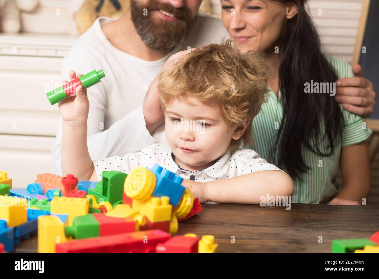 Kid with busy face plays with plastic bricks on light background ...