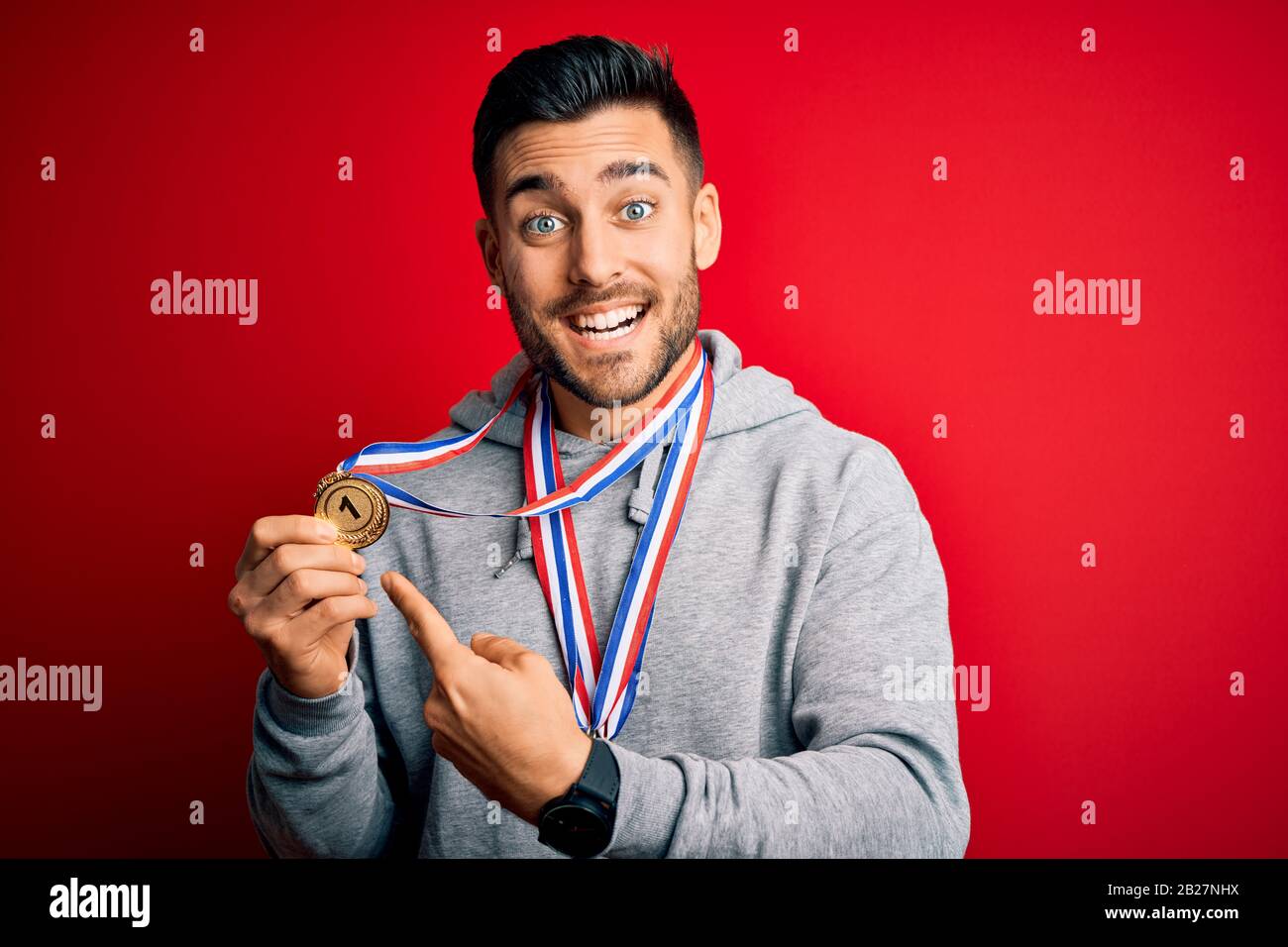 Young handsome succesful man winning medals standing over isolated red ...