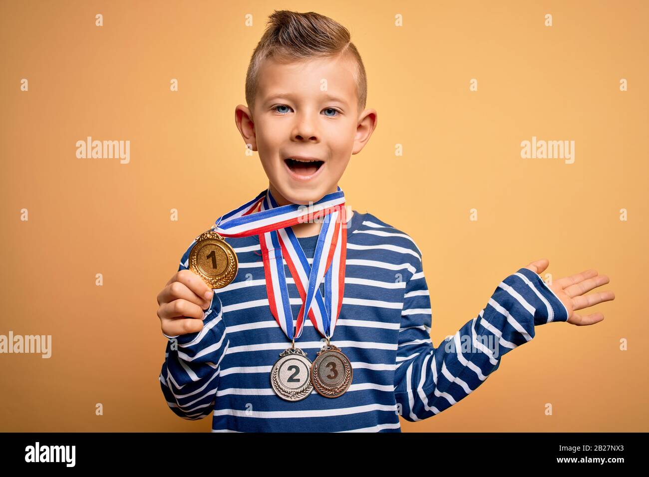 Young little caucasian winner kid wearing award competition medals over ...
