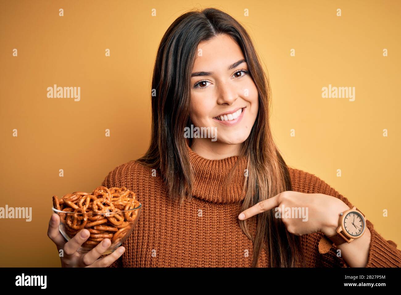Young beautiful girl eating baked german pretzel standing over isolated ...