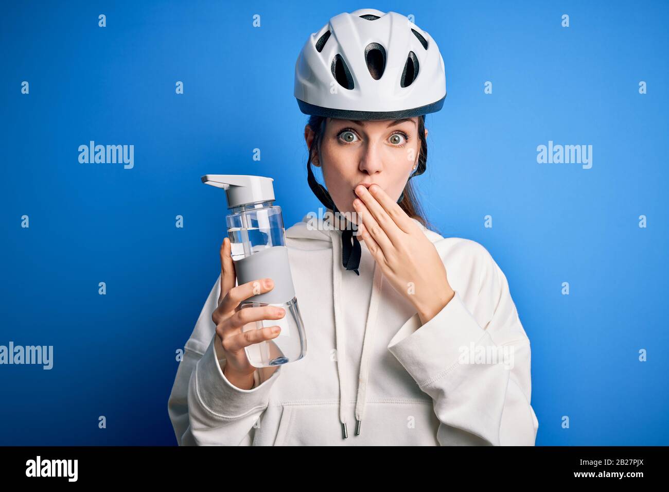 Young beautiful redhead cyclist woman wearing bike helmet drinkjng ...