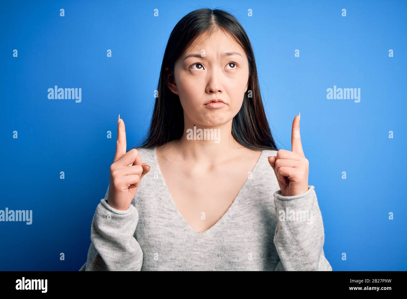 Young beautiful asian woman wearing casual sweater standing over blue ...