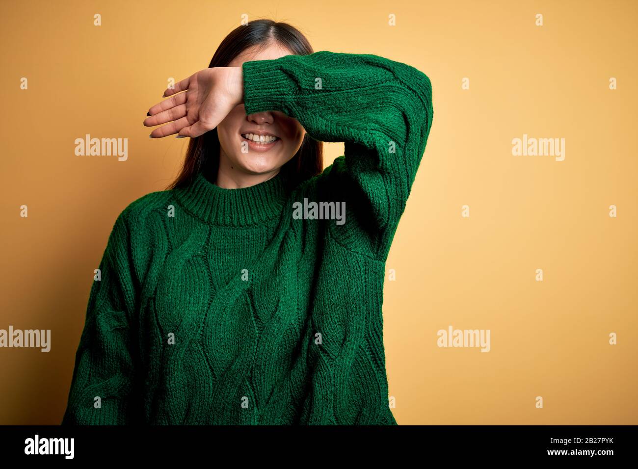 Young beautiful asian woman wearing green winter sweater over yellow ...
