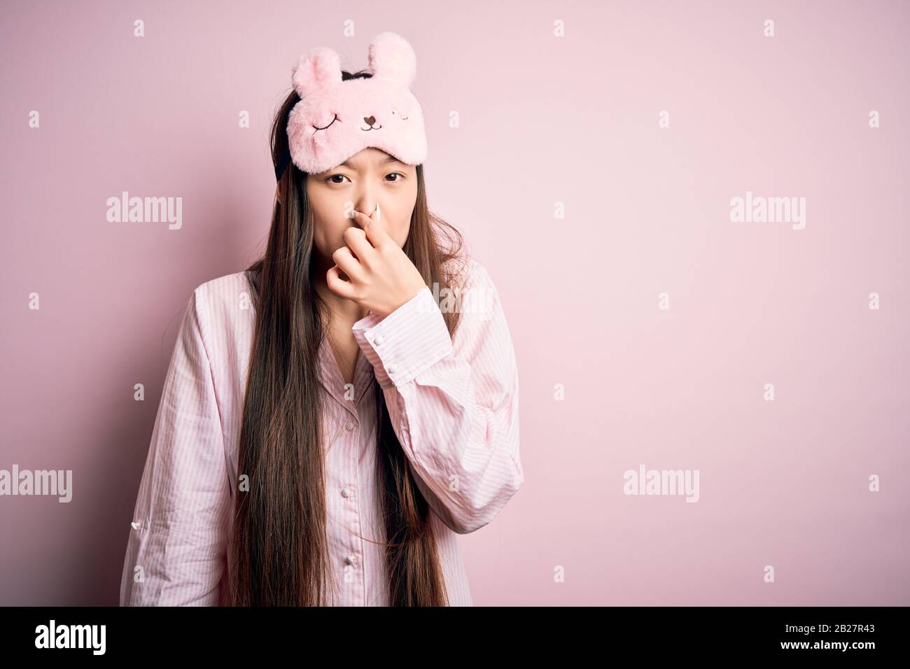 Young asian woman wearing pajama and sleep mask over pink isolated ...