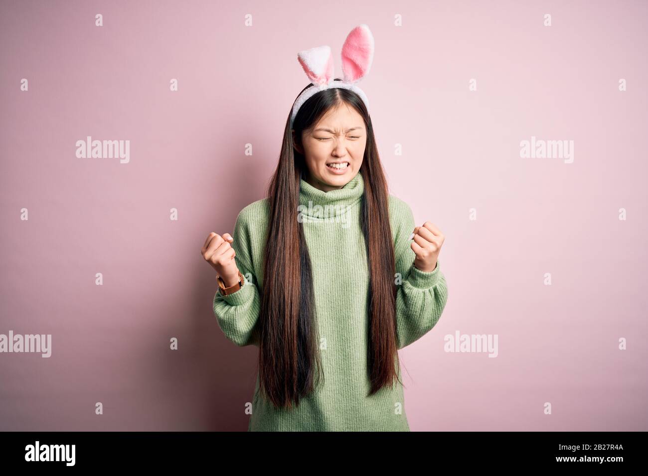 Young asian woman wearing cute easter bunny ears over pink background ...