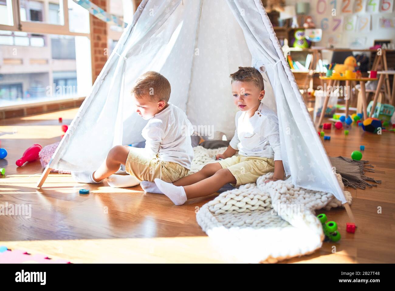 Adorable blonde twins playing inside tipi around lots of toys at ...