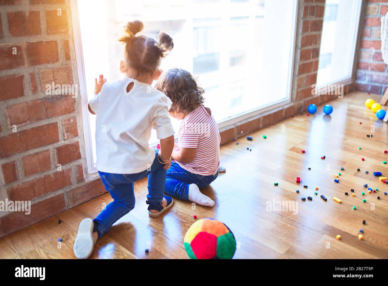 Adorable toddlers looking through the window around lots of toys at ...