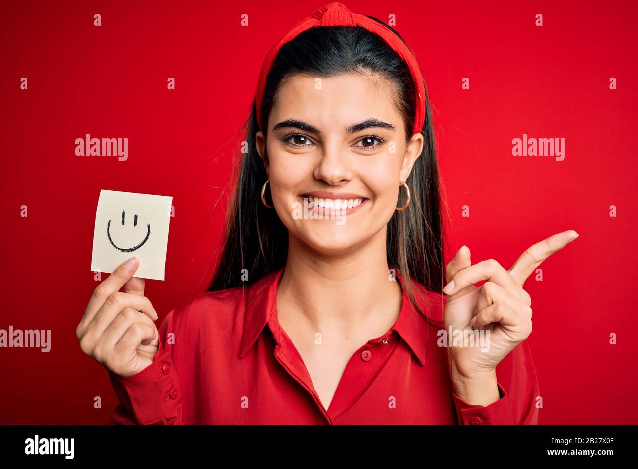 Young beautiful brunette woman holding reminder paper with smile emoji ...