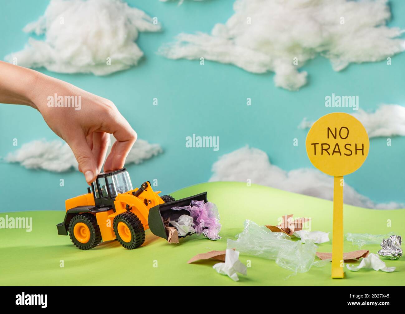 Child's hand playing with a toy truck collecting garbage on the lawn ...