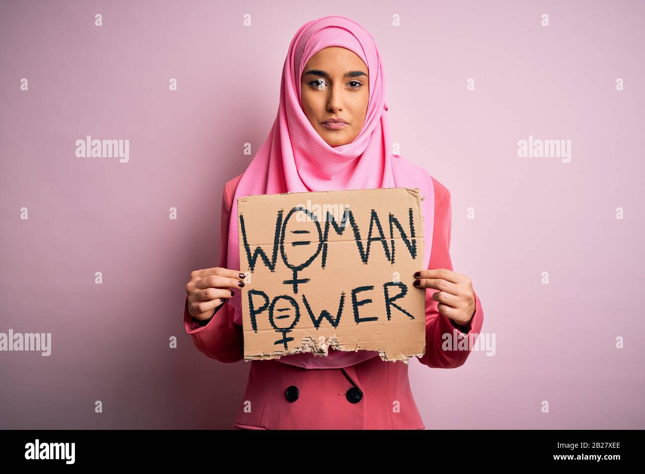 Young activist arab woman wearing pink muslim hijab holding banner with ...
