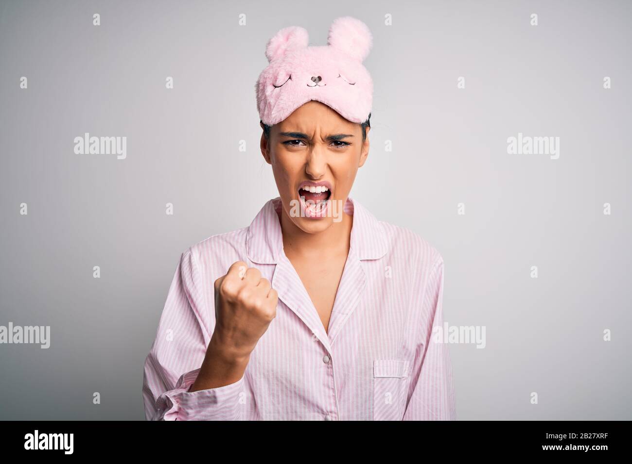 Young beautiful brunette woman wearing pajama and sleep mask over white ...