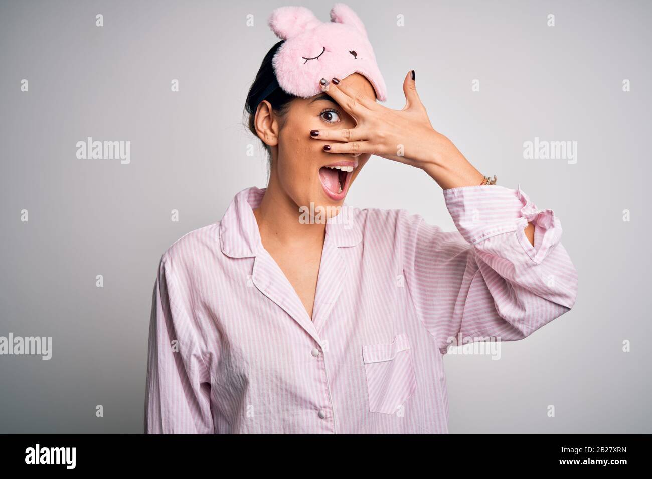 Young beautiful brunette woman wearing pajama and sleep mask over white ...
