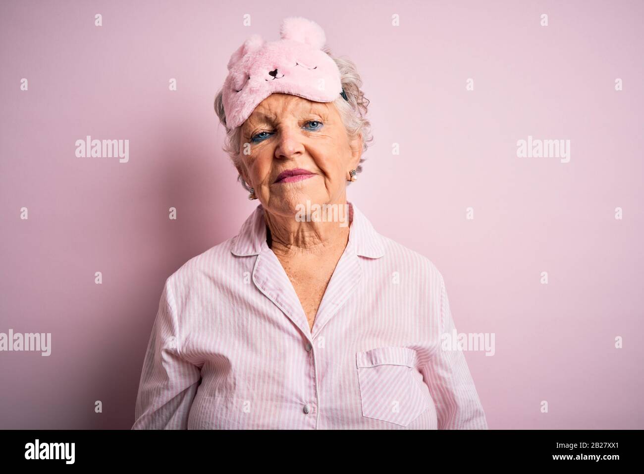 Senior beautiful woman wearing sleep mask and pajama over isolated pink ...
