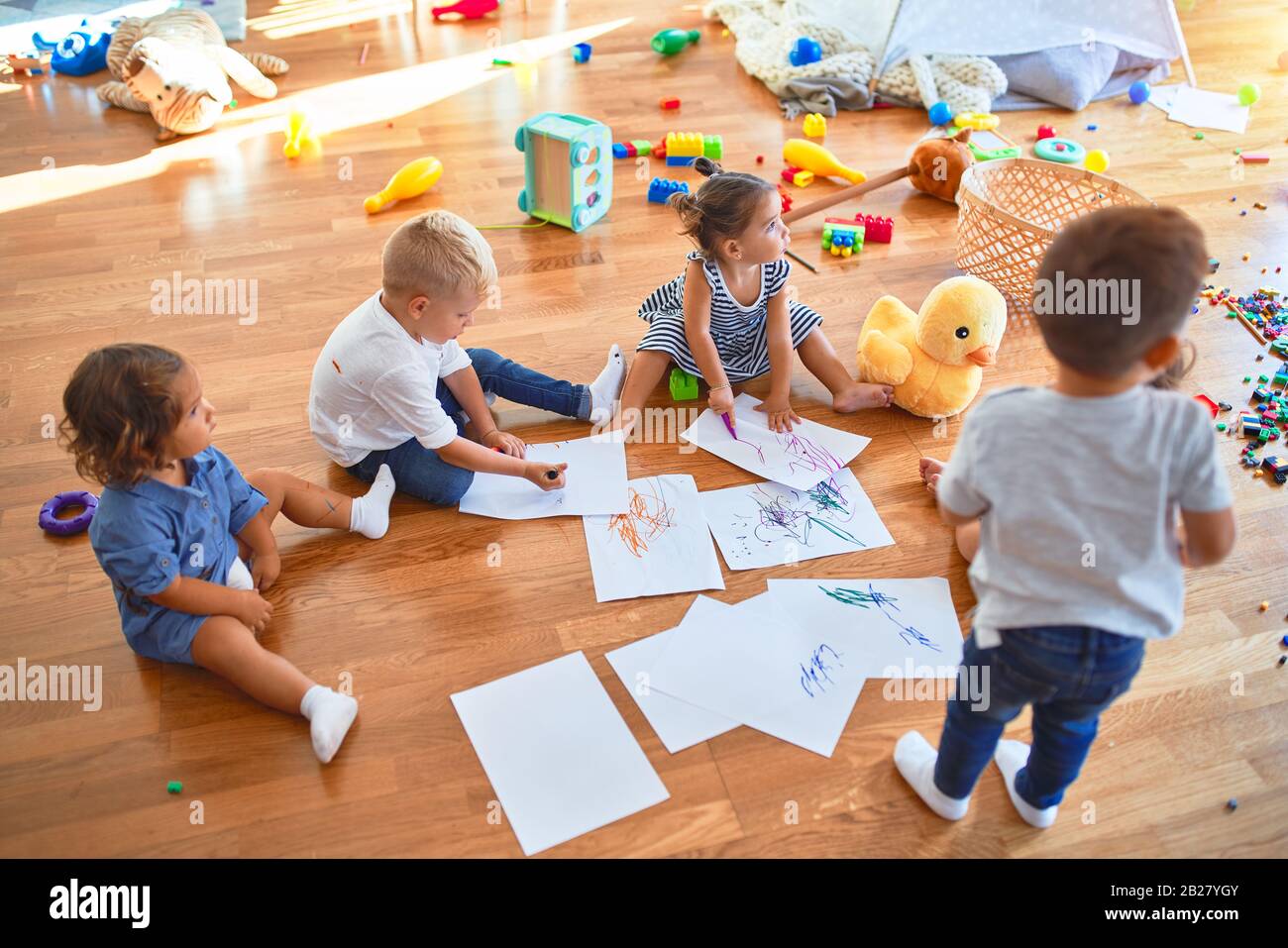 Adorable group of toddlers sitting on the floor drawing using paper and ...