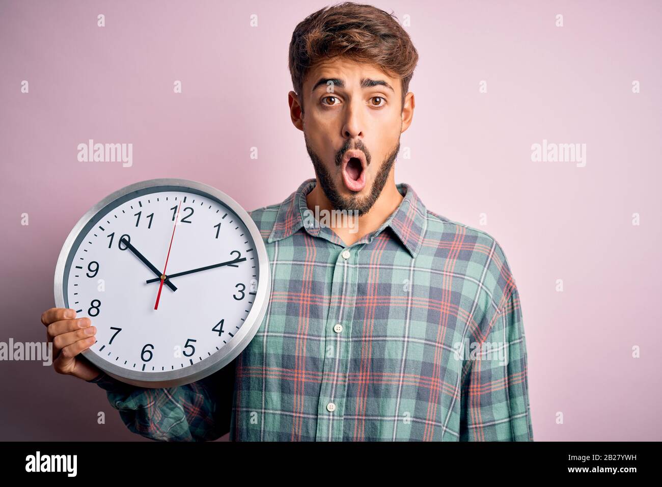 Young man with beard doing countdown using big clock over isolated pink ...