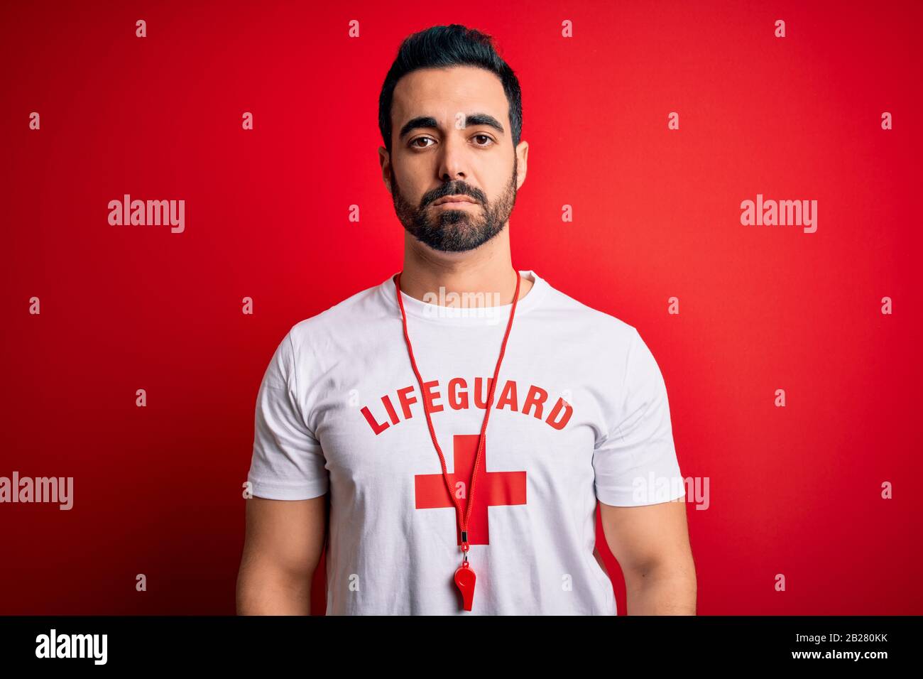 Young handsome lifeguard man with beard wearing whistle over isolated ...