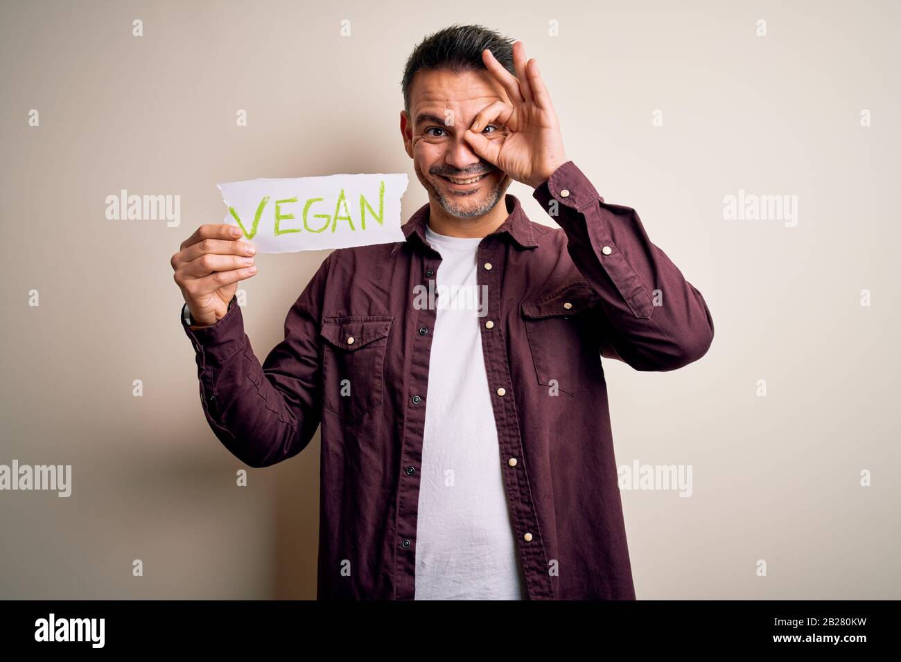 Young handsome veggie man holding paper with vegan message over white ...