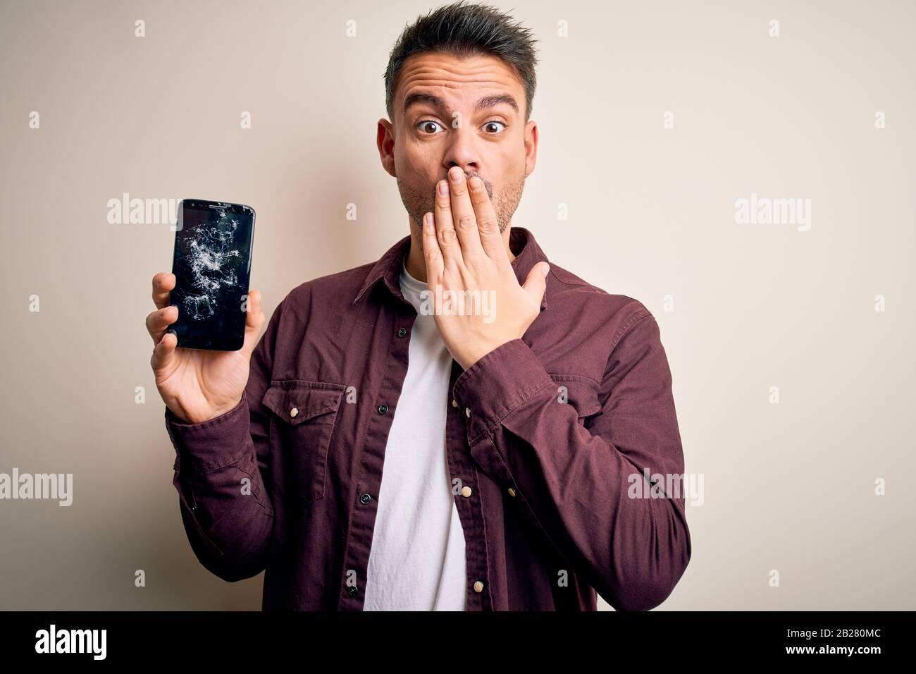Young handsome man holding broken smartphone showing craked screen ...