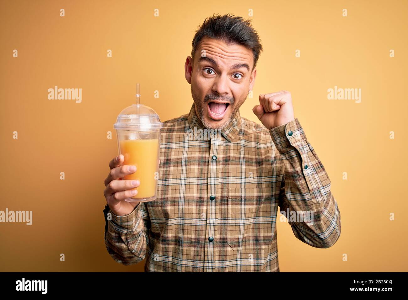 Young handsome man drinking healthy orange juice using straw over ...