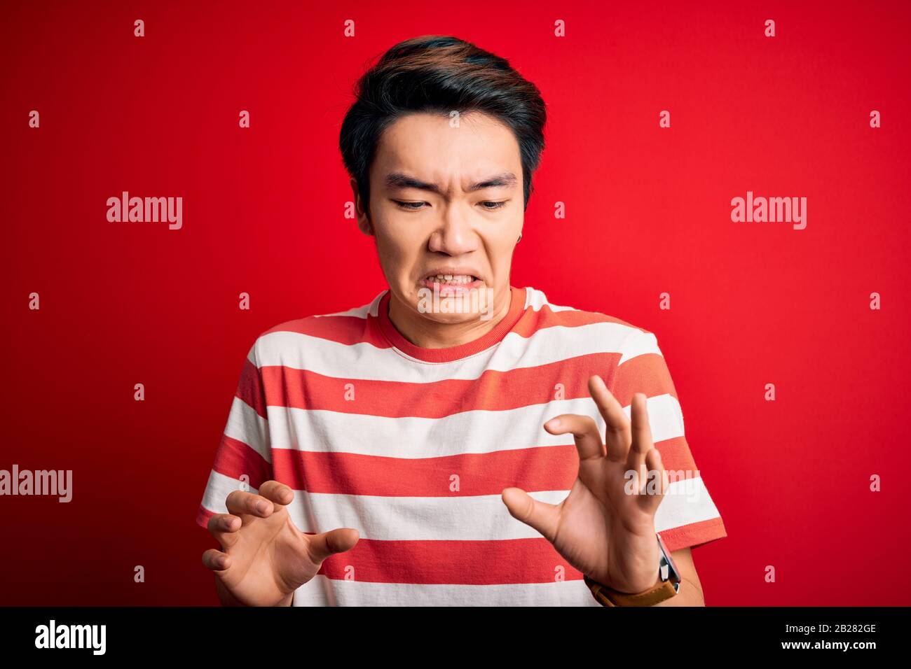 Young handsome chinese man wearing casual striped t-shirt standing over ...