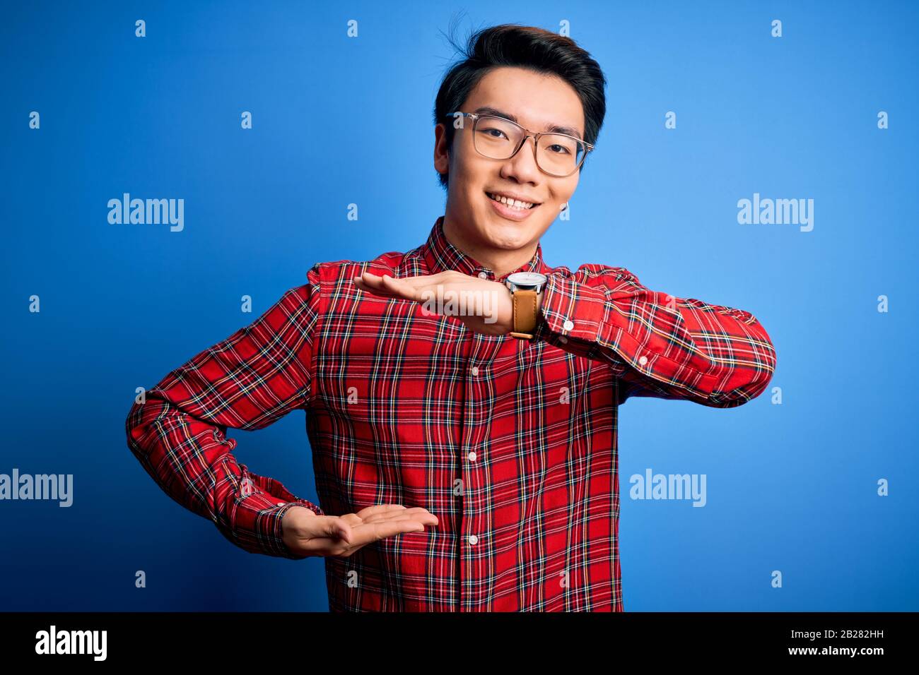 Young handsome chinese man wearing casual shirt and glasses over blue ...