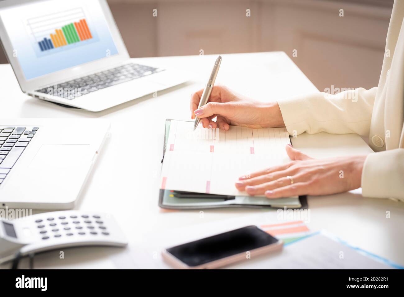 Close-up shot of a businesswoman using a laptop and writing notes at ...