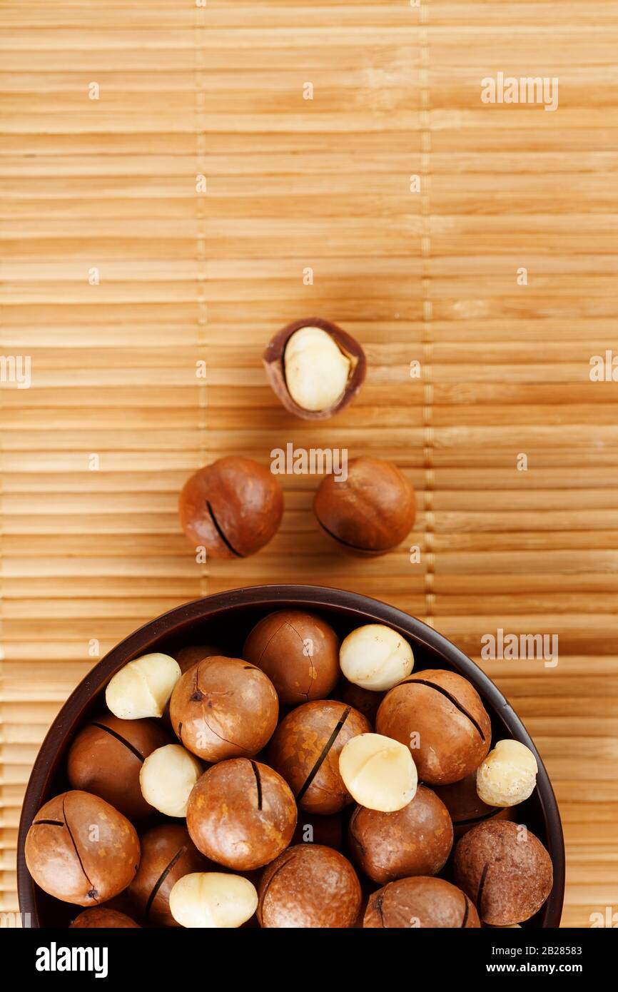 Macadamia nut on bamboo texture in a wooden cup, peeled and not peeled ...