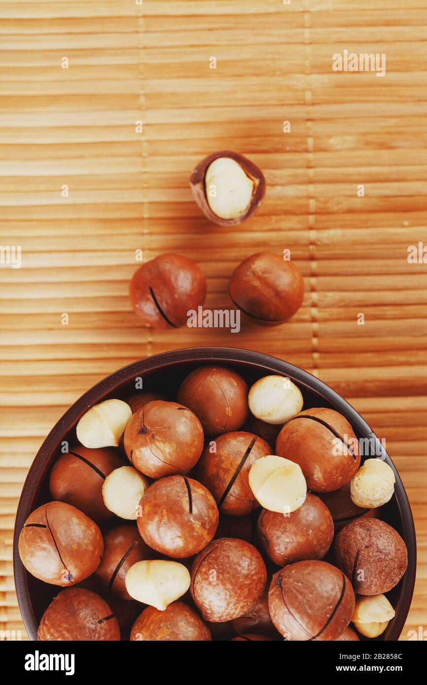 Macadamia nut on bamboo texture in a wooden cup, peeled and not peeled ...