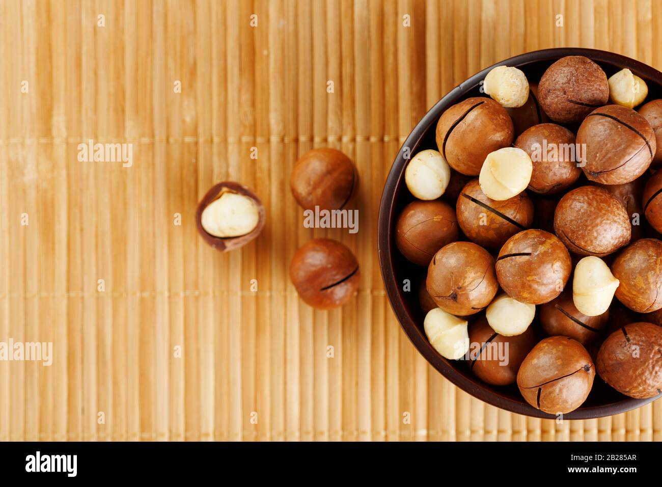 Macadamia nut on bamboo texture in a wooden cup, peeled and not peeled ...