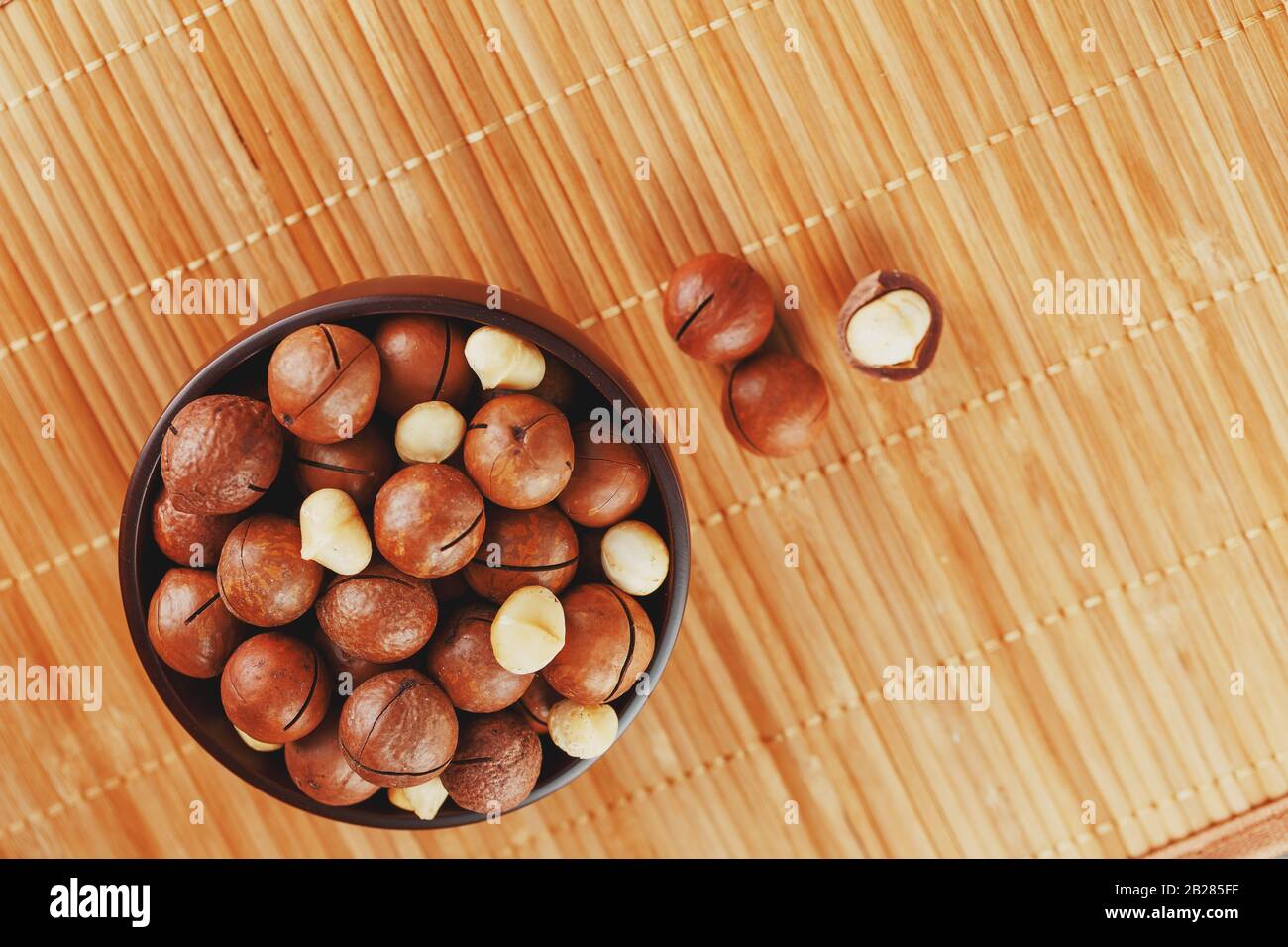 Macadamia nut on bamboo texture in a wooden cup, peeled and not peeled ...