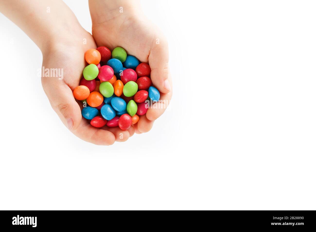 Multicolored candies in the hands of a child on a white isolated ...