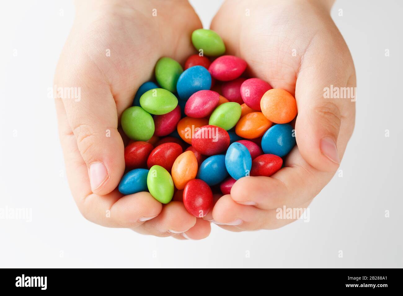 Multicolored candies in the hands of a child on a white isolated ...