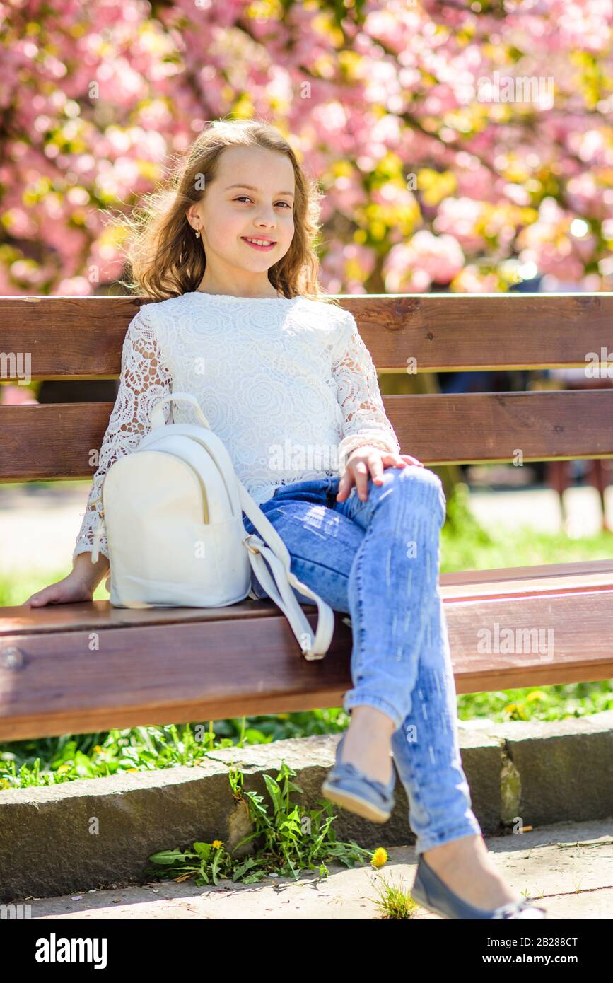 Girl on smiling face sits on bench, sakura tree on background ...