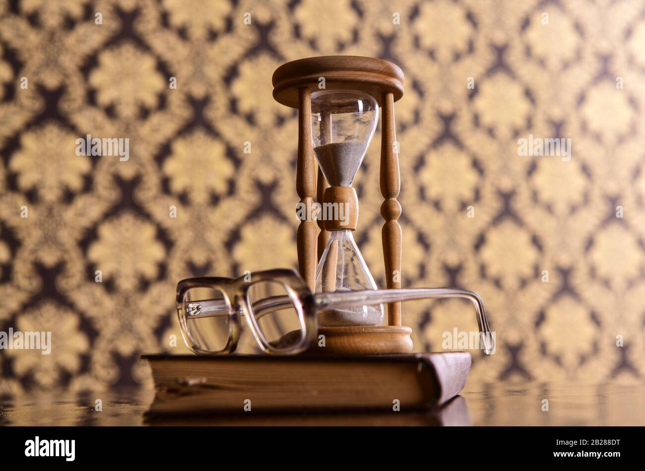 Hourglass, old book and eyeglasses on wooden table, pattern background ...