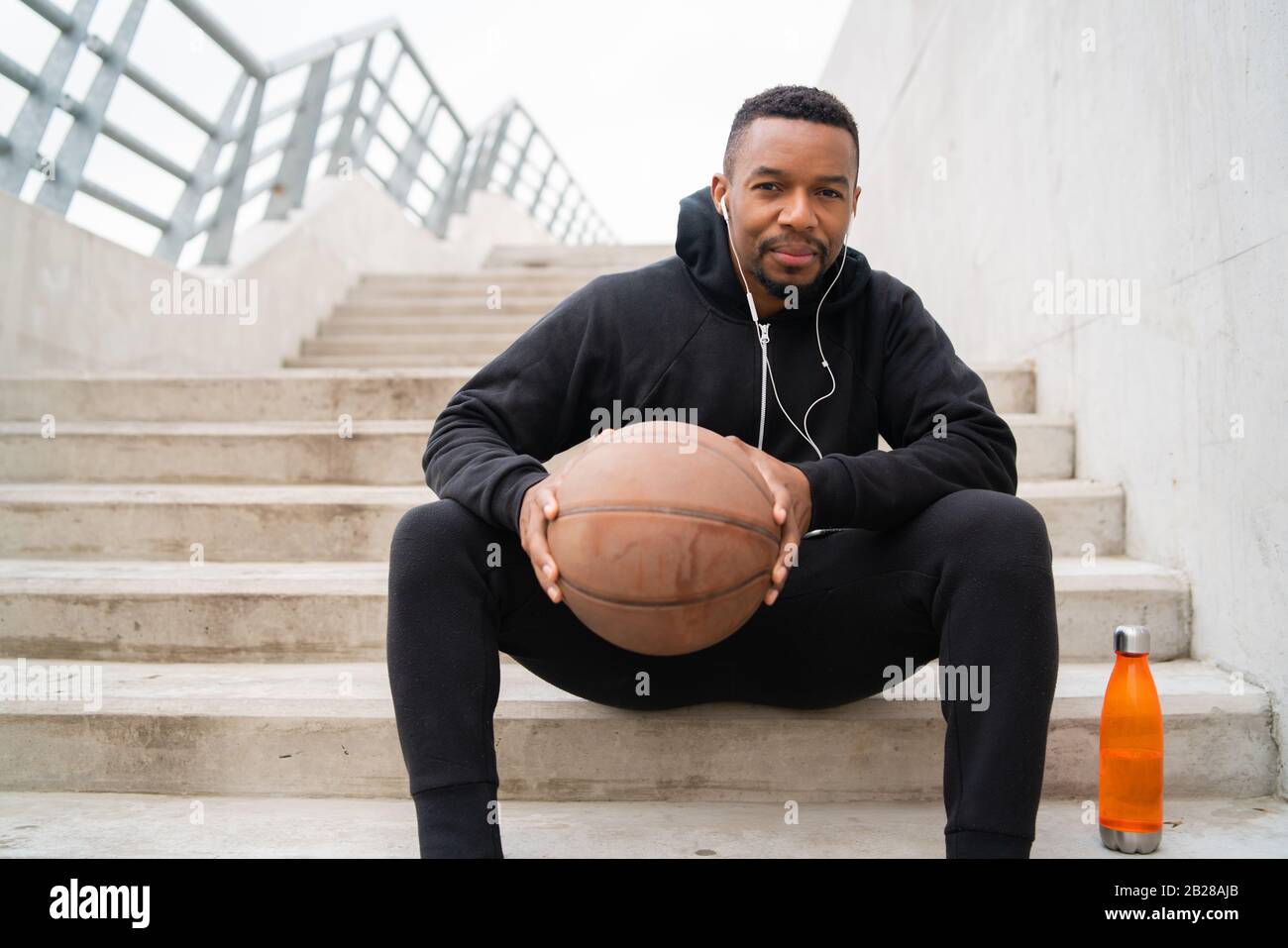 Portrait of an athletic man holding a basket ball while sitting on ...