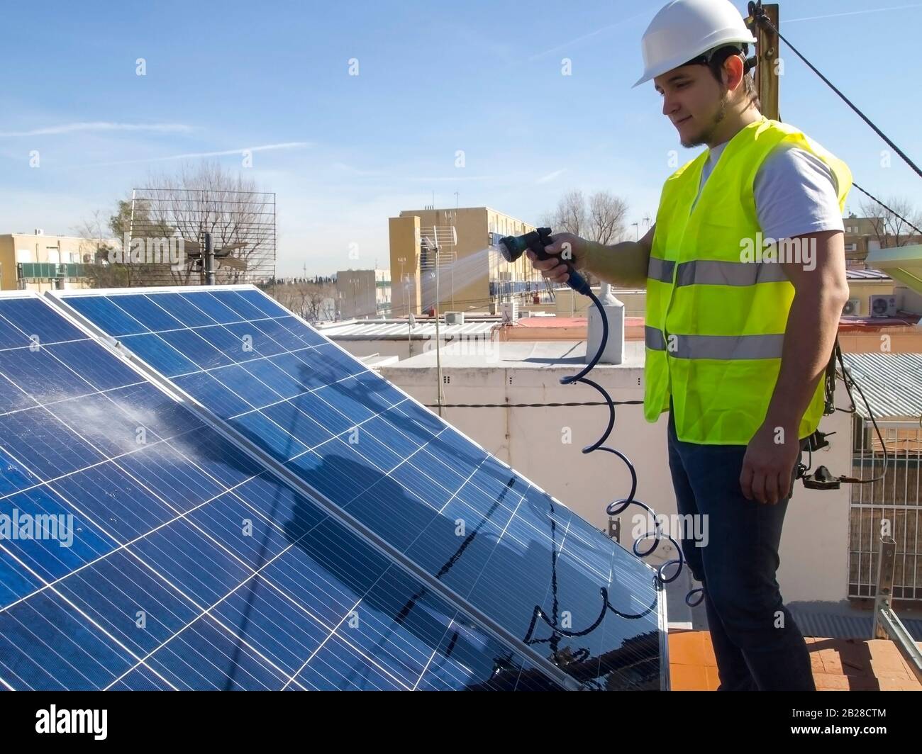 Caucasian attractive young technician cleaning solar panels with a hose ...