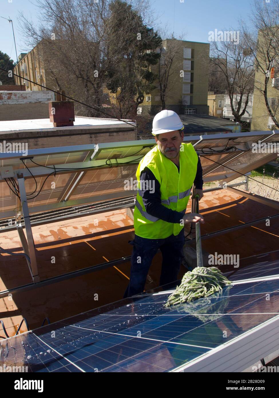 Caucasian seasoned technician cleaning the solar panels with a mop ...