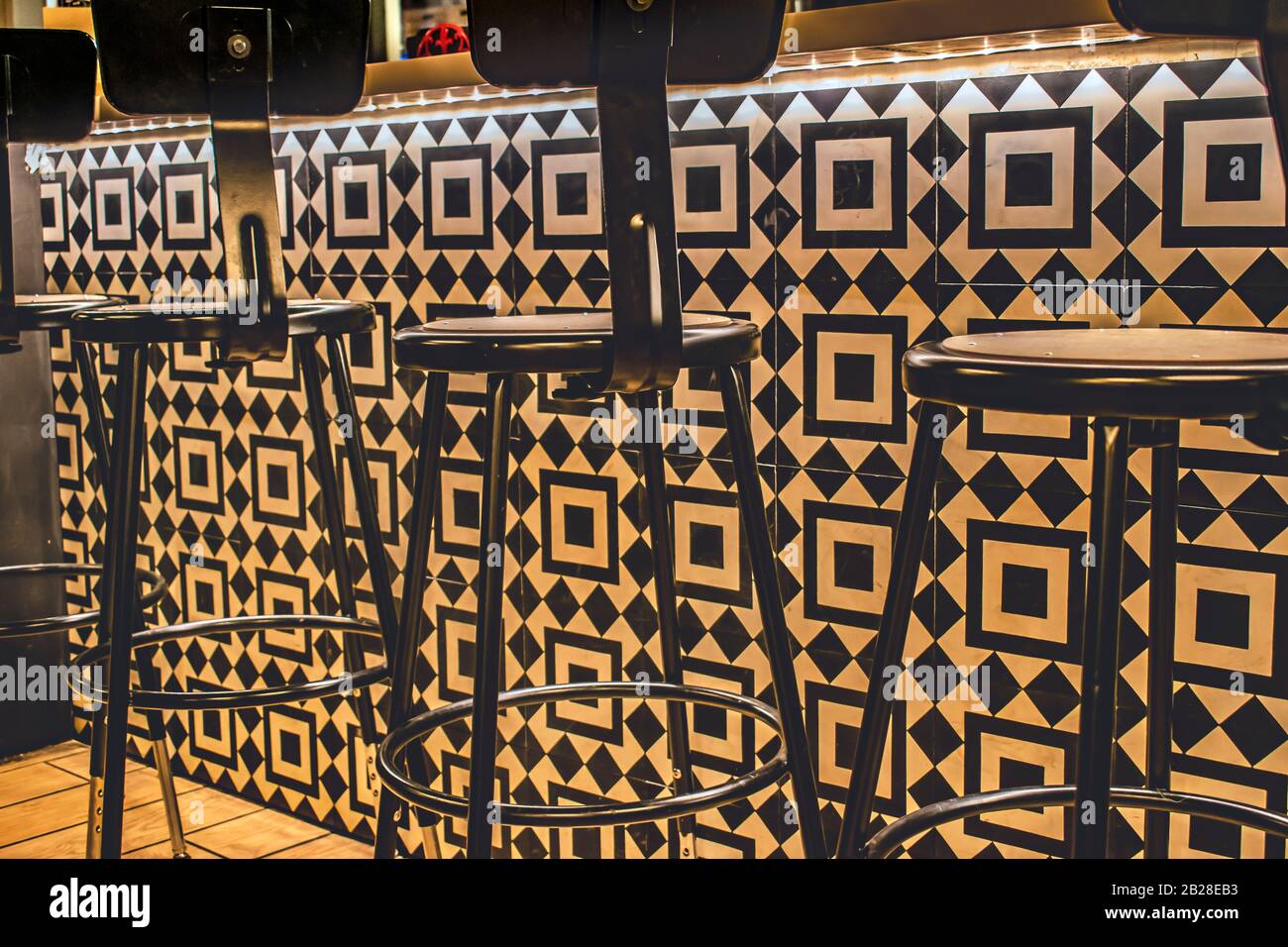 Black bar stools against a black and white mosaic tile wall under the ...