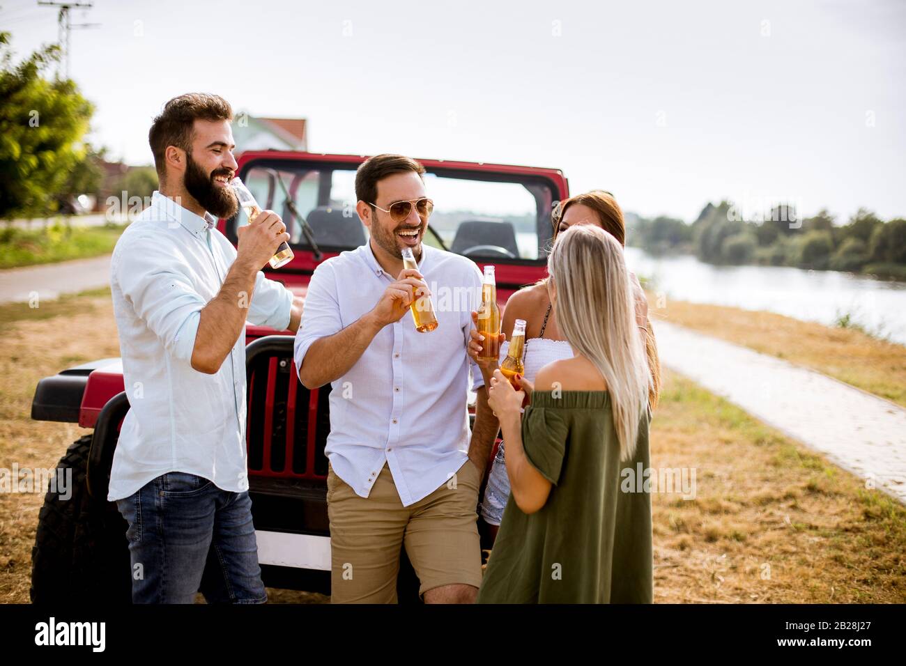 Group of young people drinking and having fun by car outdoor on a sunny ...