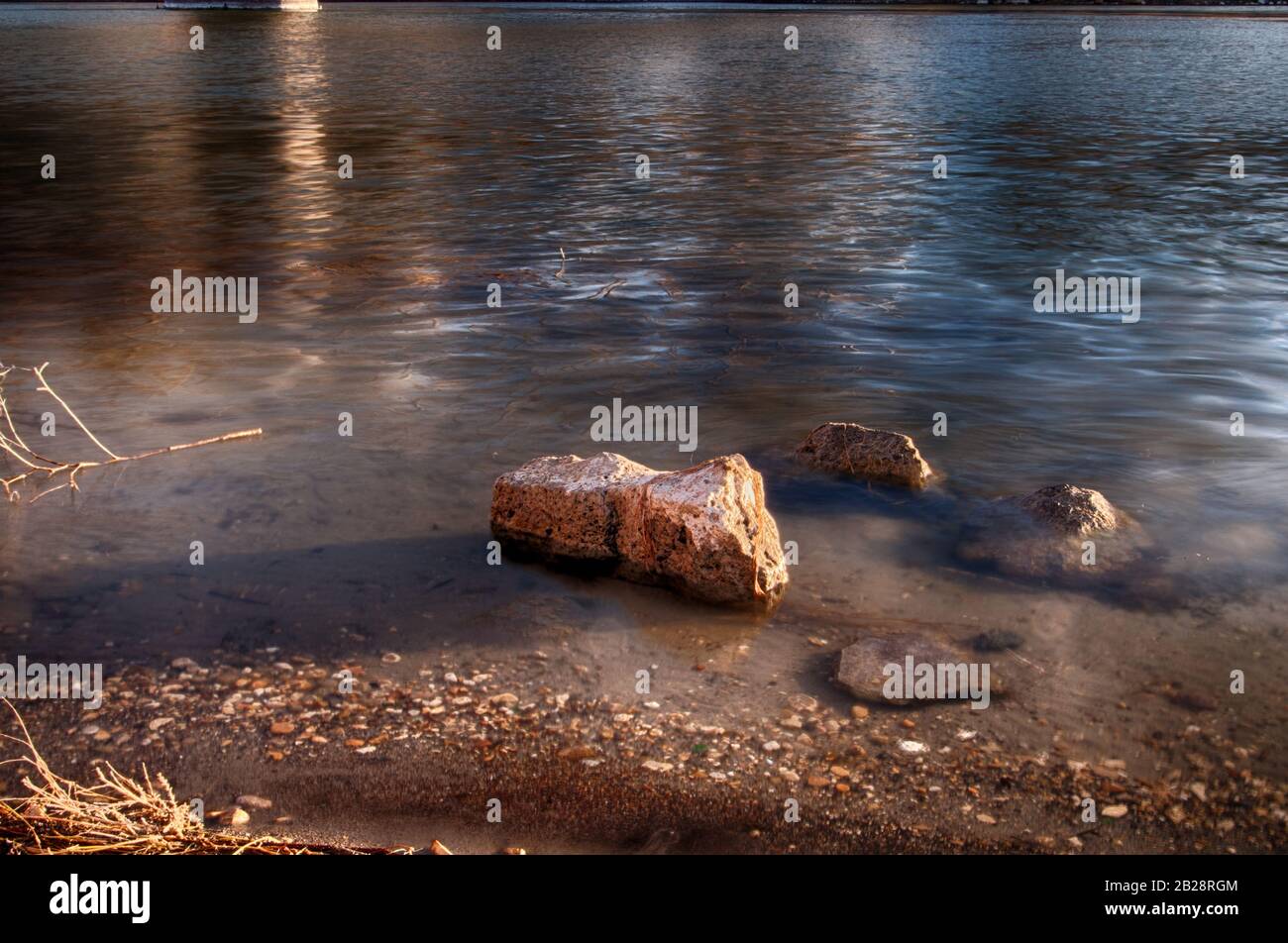 Sandstone rocks sticking out of the reflective water on the bank of the ...