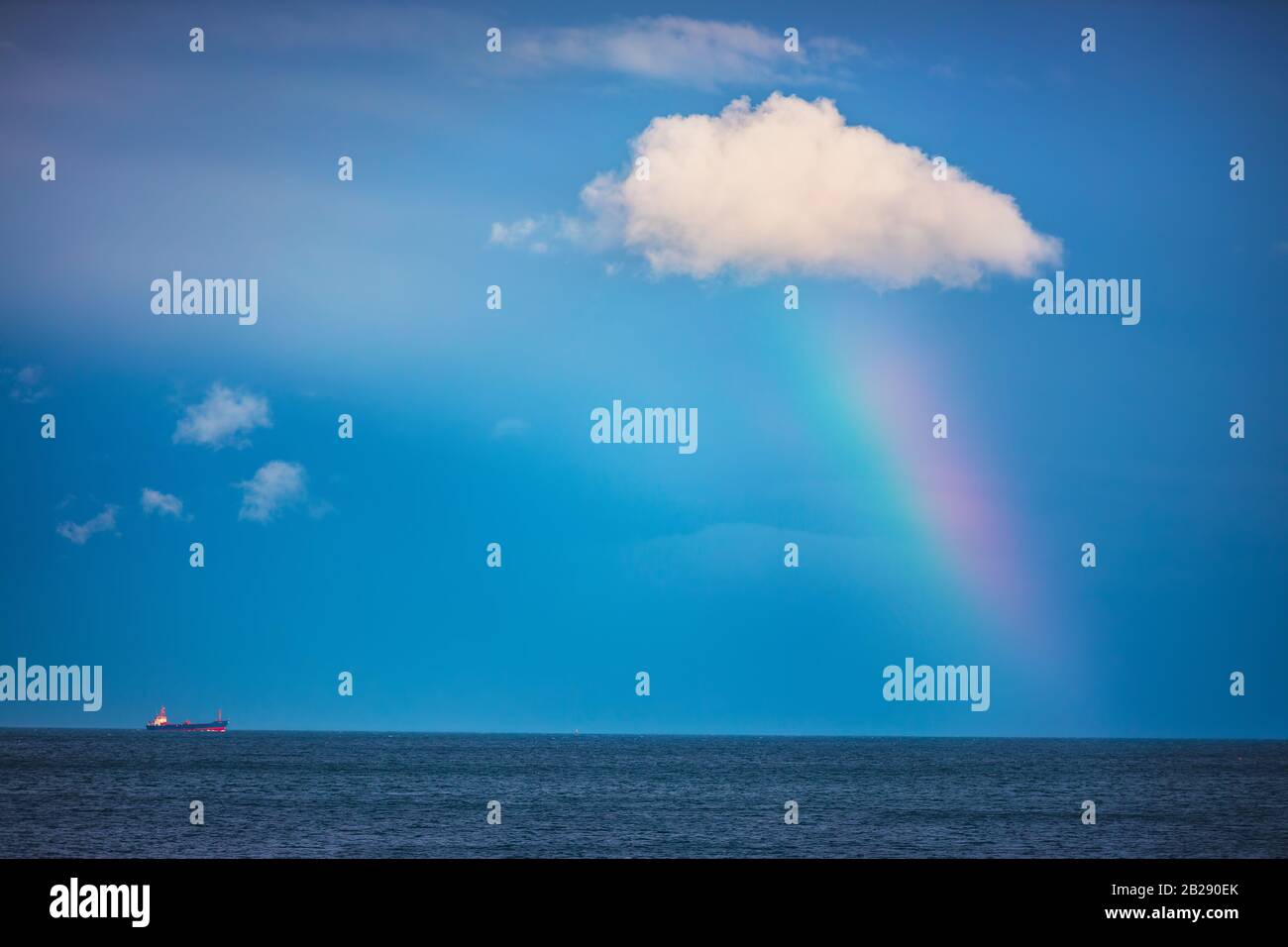 Rainbow in the sea and sailing cargo ship Stock Photo - Alamy