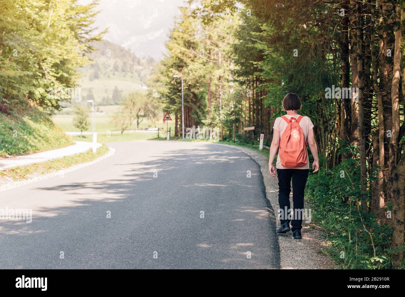 Female hiker walking by the road through countryside, rear view of ...